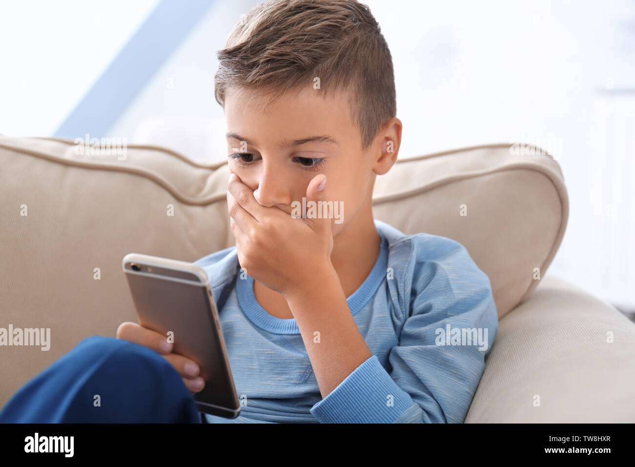 Upset little boy with smartphone at home Stock Photo - Alamy