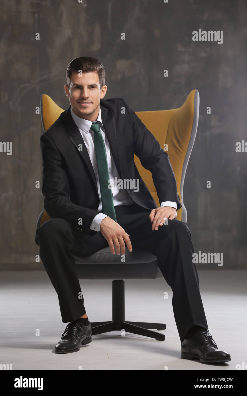 Handsome young man sitting in armchair on dark background Stock Photo ...