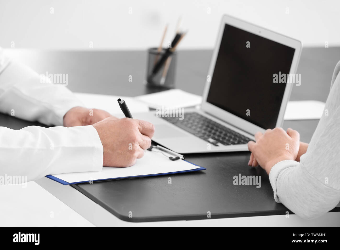 Male doctor filling up application form while consulting patient in ...
