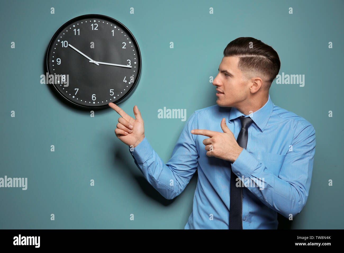 Handsome manager looking at clock hanging on wall Stock Photo - Alamy