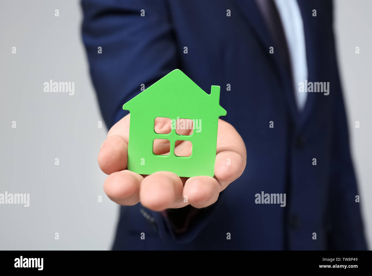Real estate agent holding house model on grey background Stock Photo ...