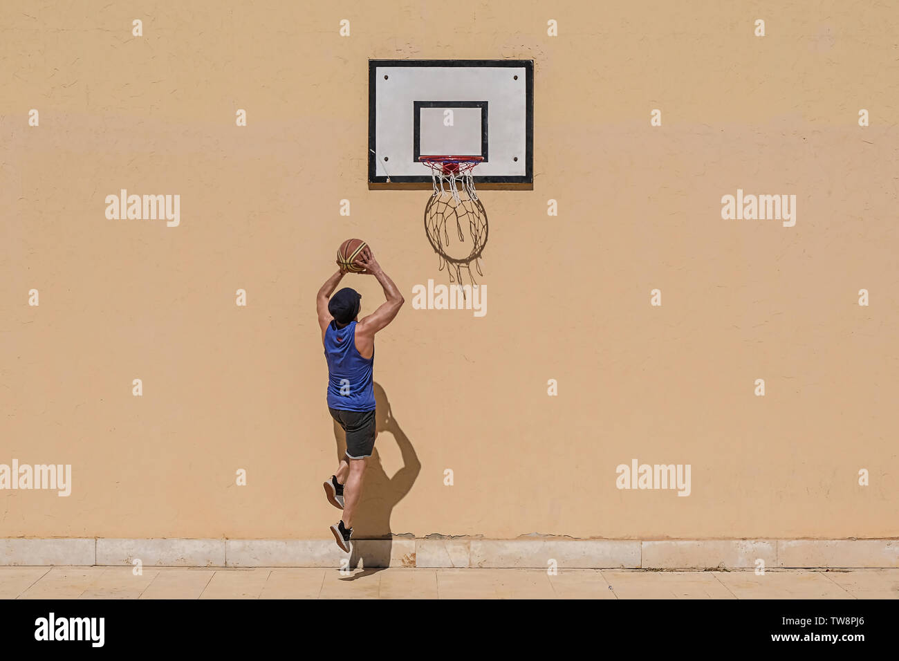 One man playing basketball on his own. The ball and net create shadows ...