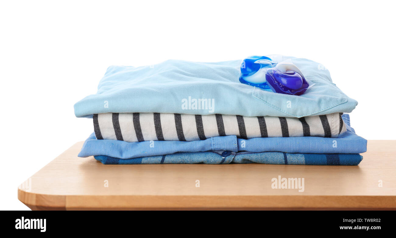 Stack of clothes and laundry pods on table against white background ...