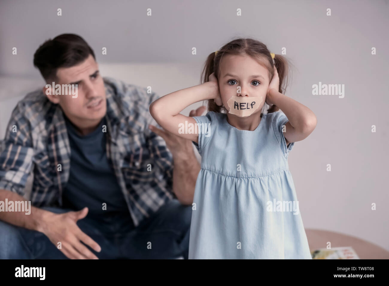 Man scolding his daughter with taped mouth and word "Help" indoors ...