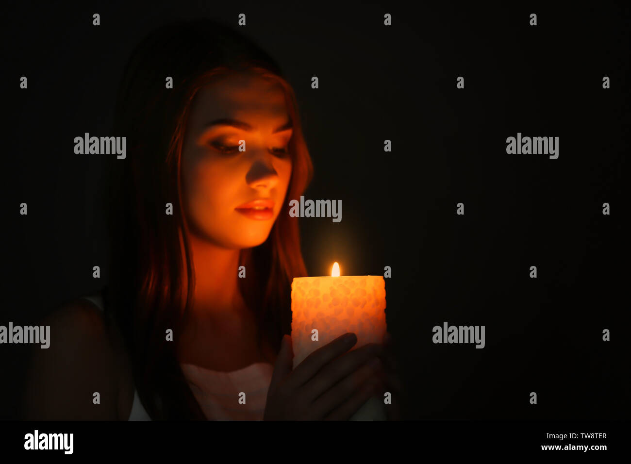 Beautiful young woman with burning candle in darkness Stock Photo - Alamy