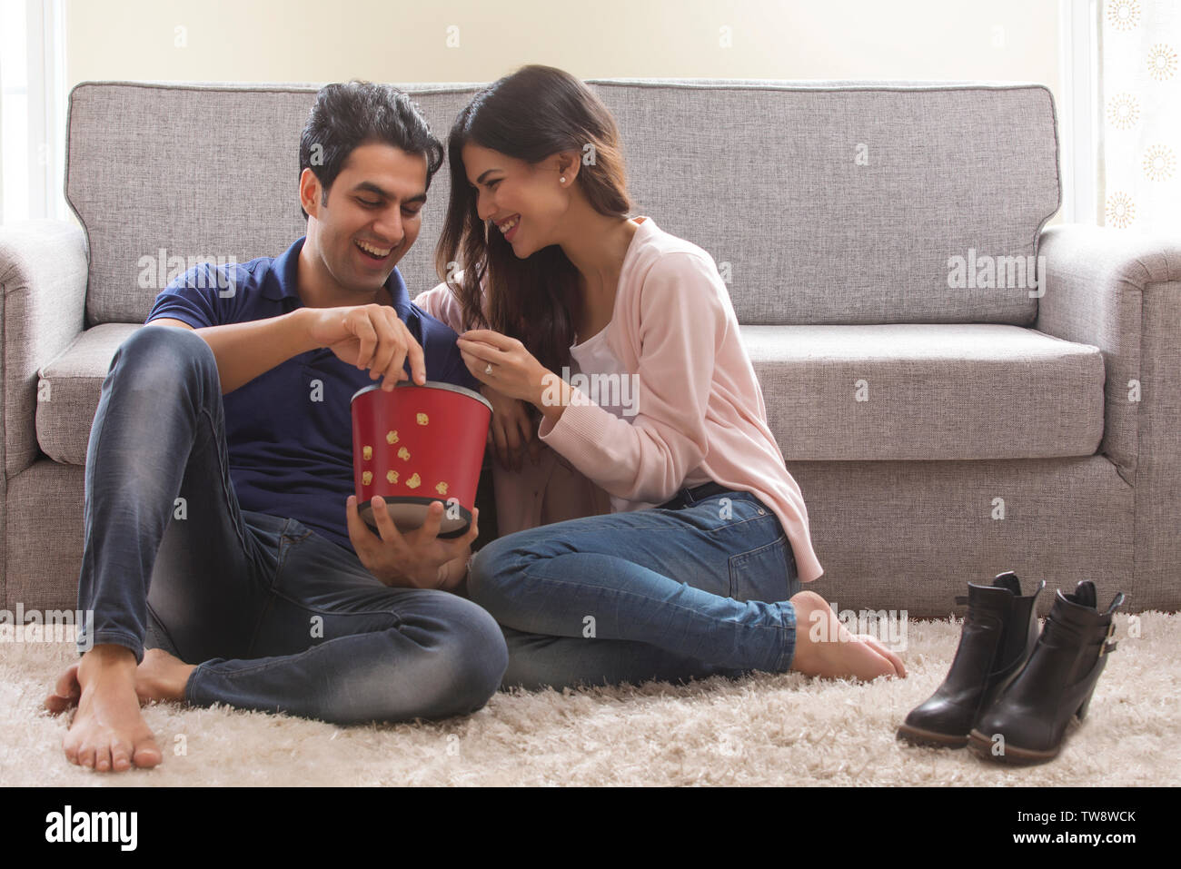 Young couple eating popcorn sitting on floor Stock Photo - Alamy