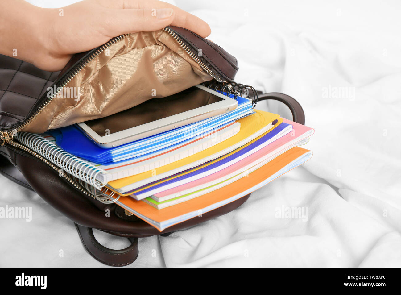 Woman opening backpack with colourful notebooks and tablet on bed Stock ...