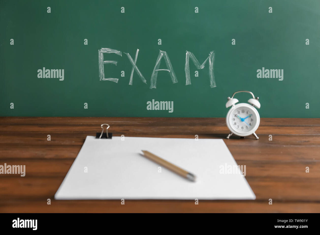 Table with alarm clock, sheets of paper and word EXAM written on ...