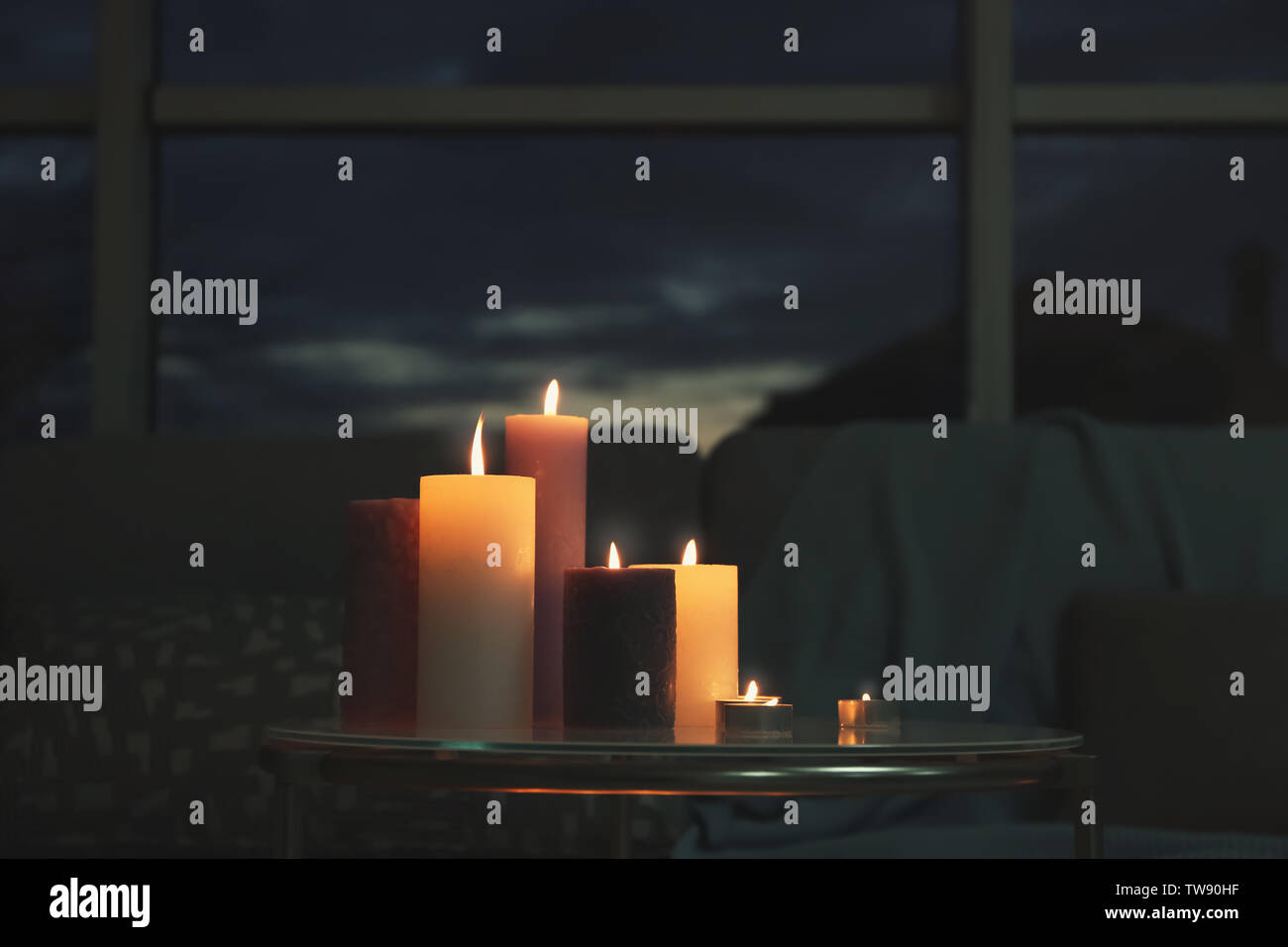 Burning candles on table in dark room Stock Photo - Alamy