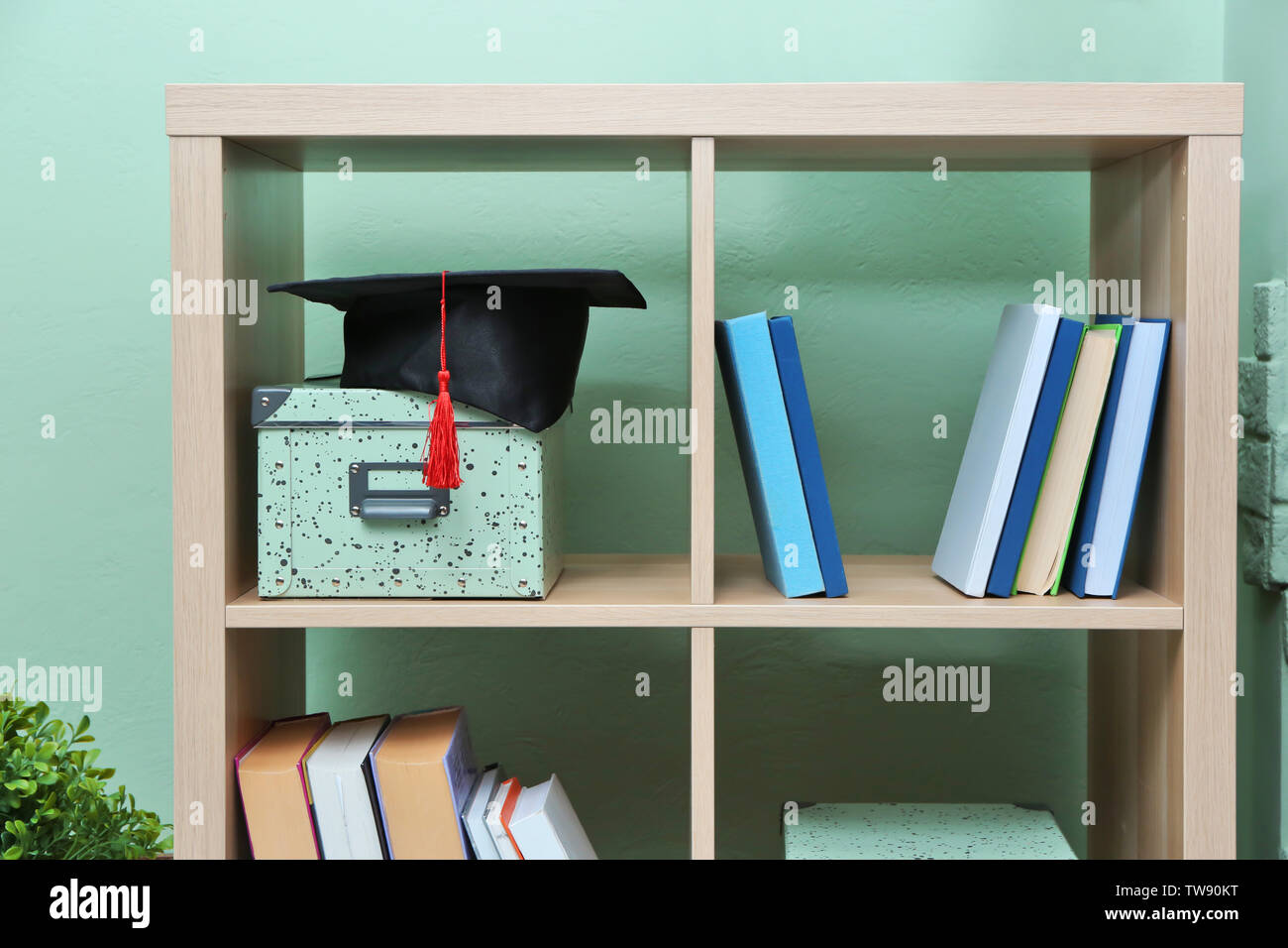 Graduation cap with textbooks on shelves indoors. Passing of exams ...
