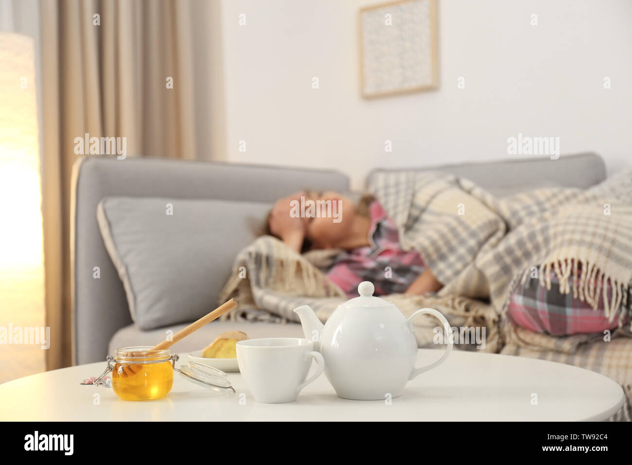 Sick woman lying on sofa. Honey and tea on table in front of her Stock ...