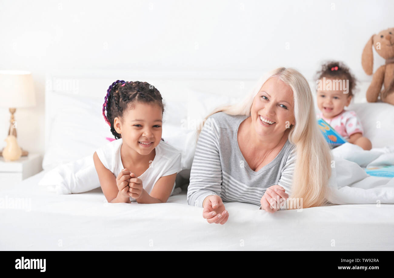 Female mature nanny with little African-American girl lying on bed ...