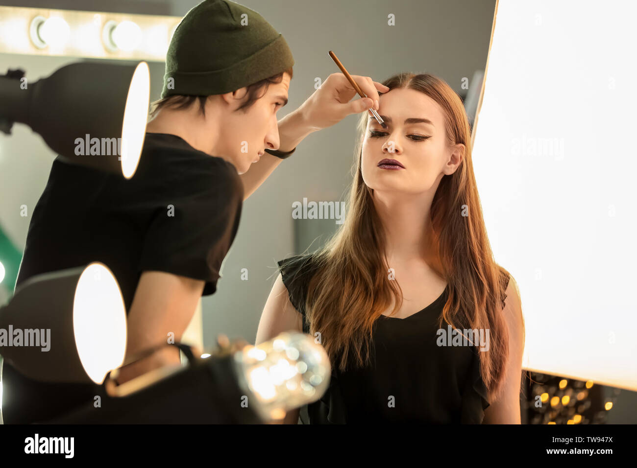 Professional artist creating makeup for beautiful model in room Stock ...