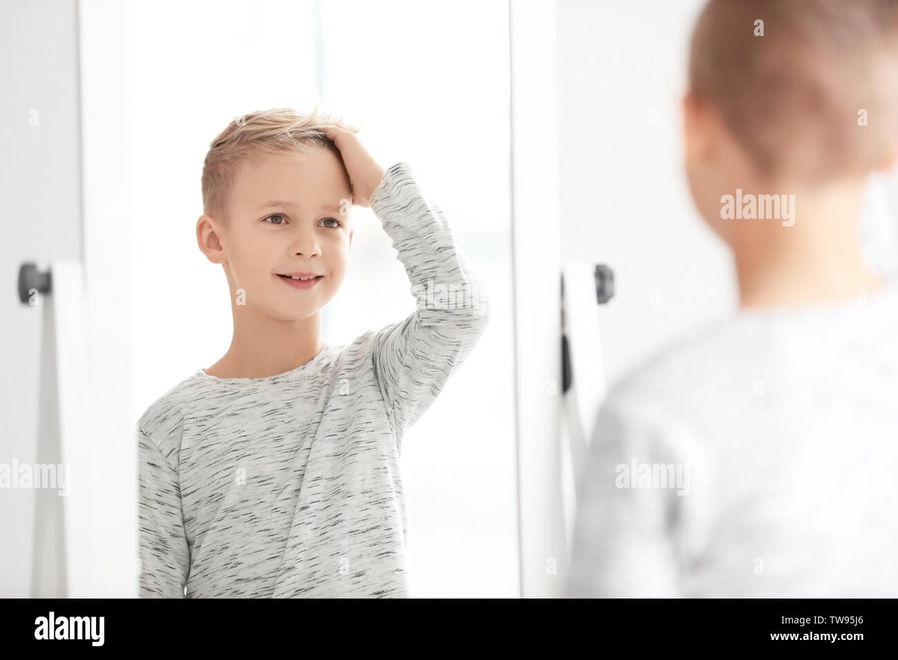Cute little boy looking at himself in mirror indoors Stock Photo - Alamy