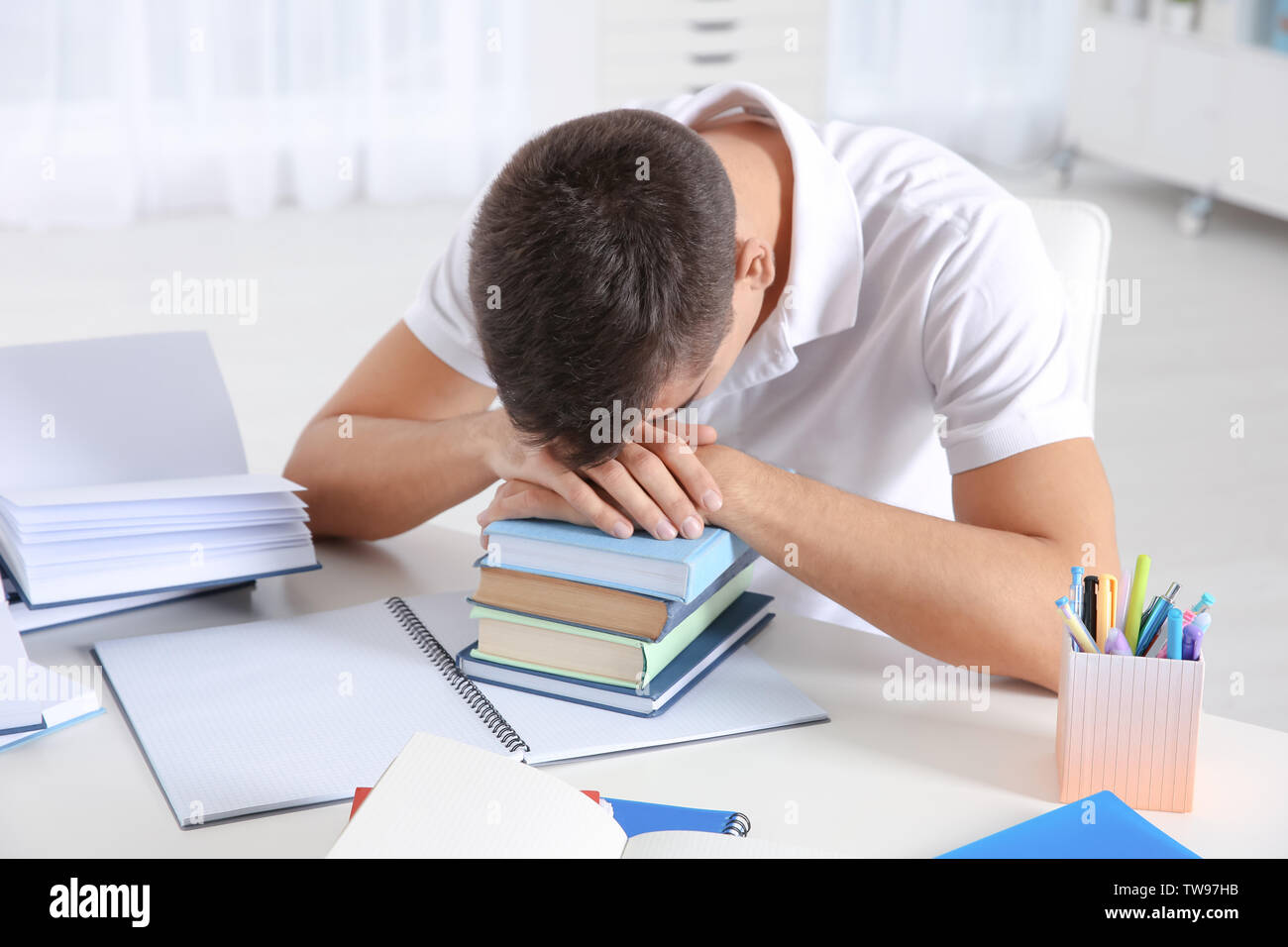 Tired student sleeping on stack of books at his desk. Preparing for ...