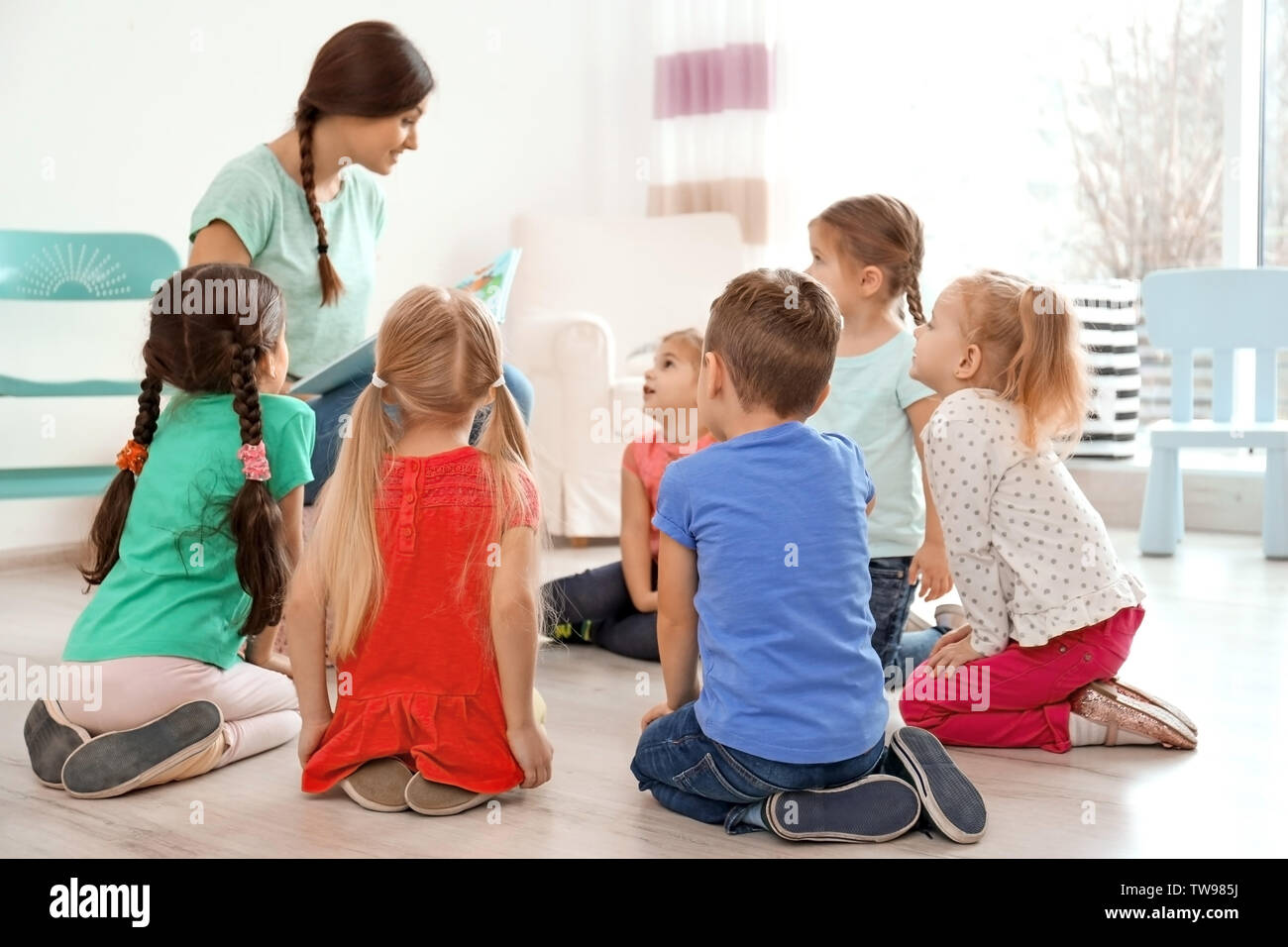 Female teacher reading book to little children in kindergarten Stock ...