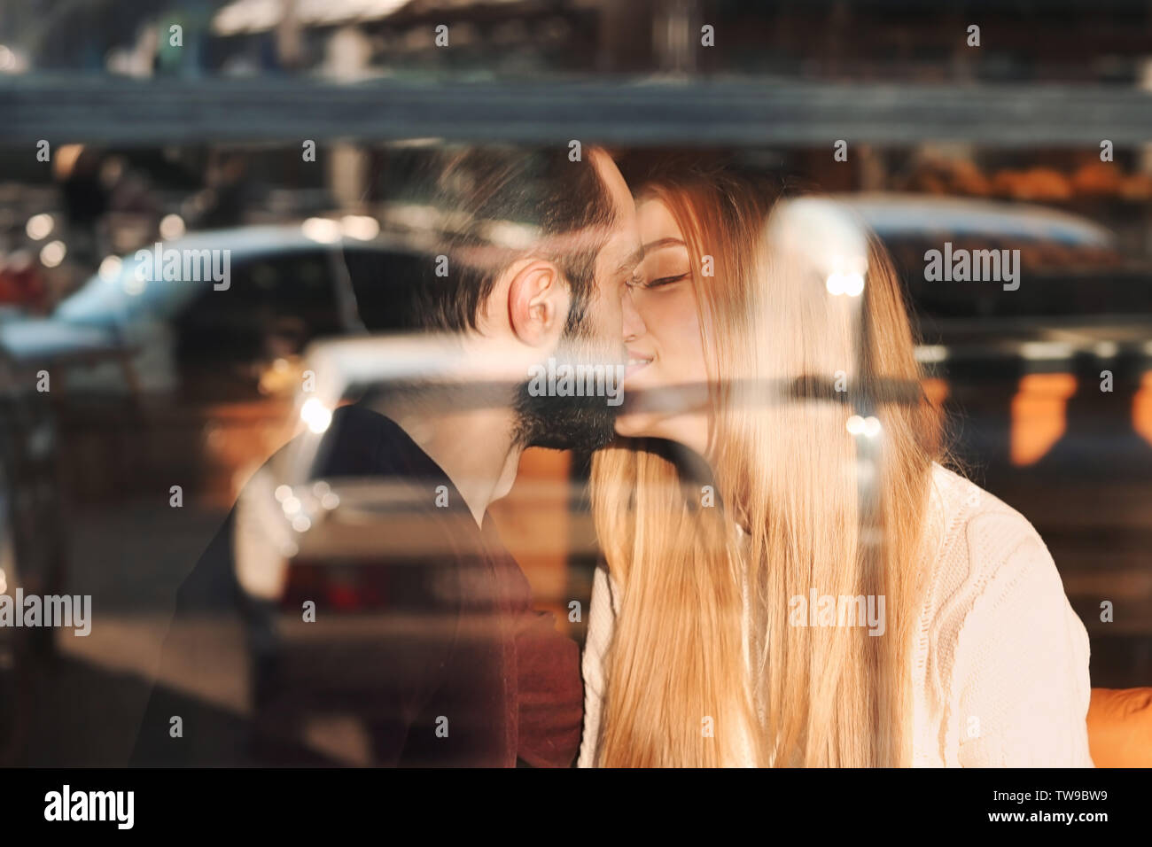 Young romantic couple kissing in cafe, view from outdoors through ...