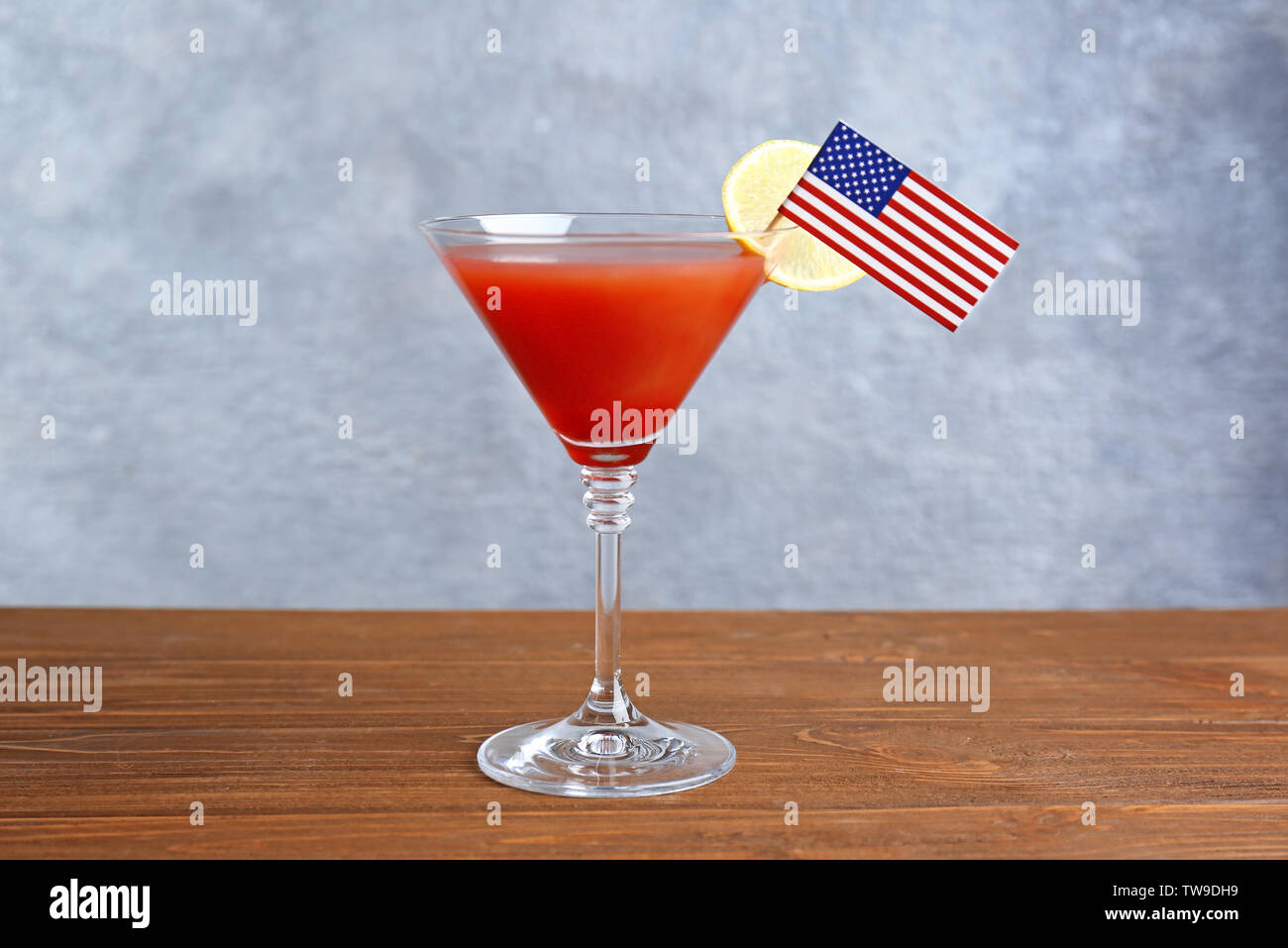 Glass of cocktail with small USA flag on table against grey background ...