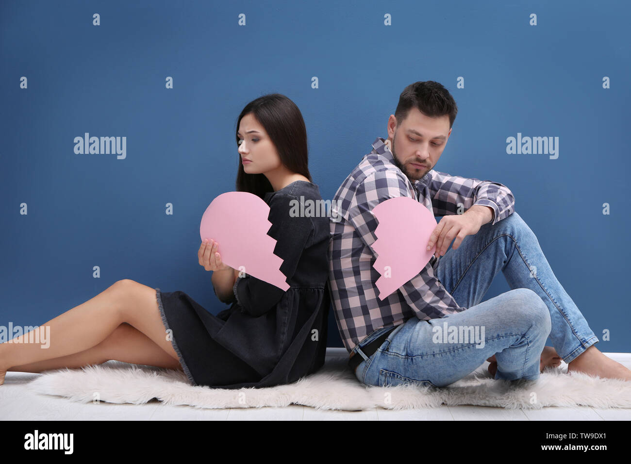 Young couple holding paper heart cut in half near color wall ...