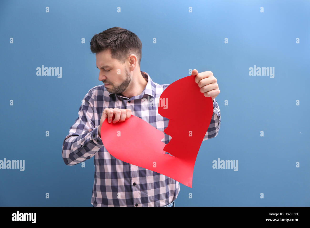 Young man tearing paper heart in half on color background. Relationship ...