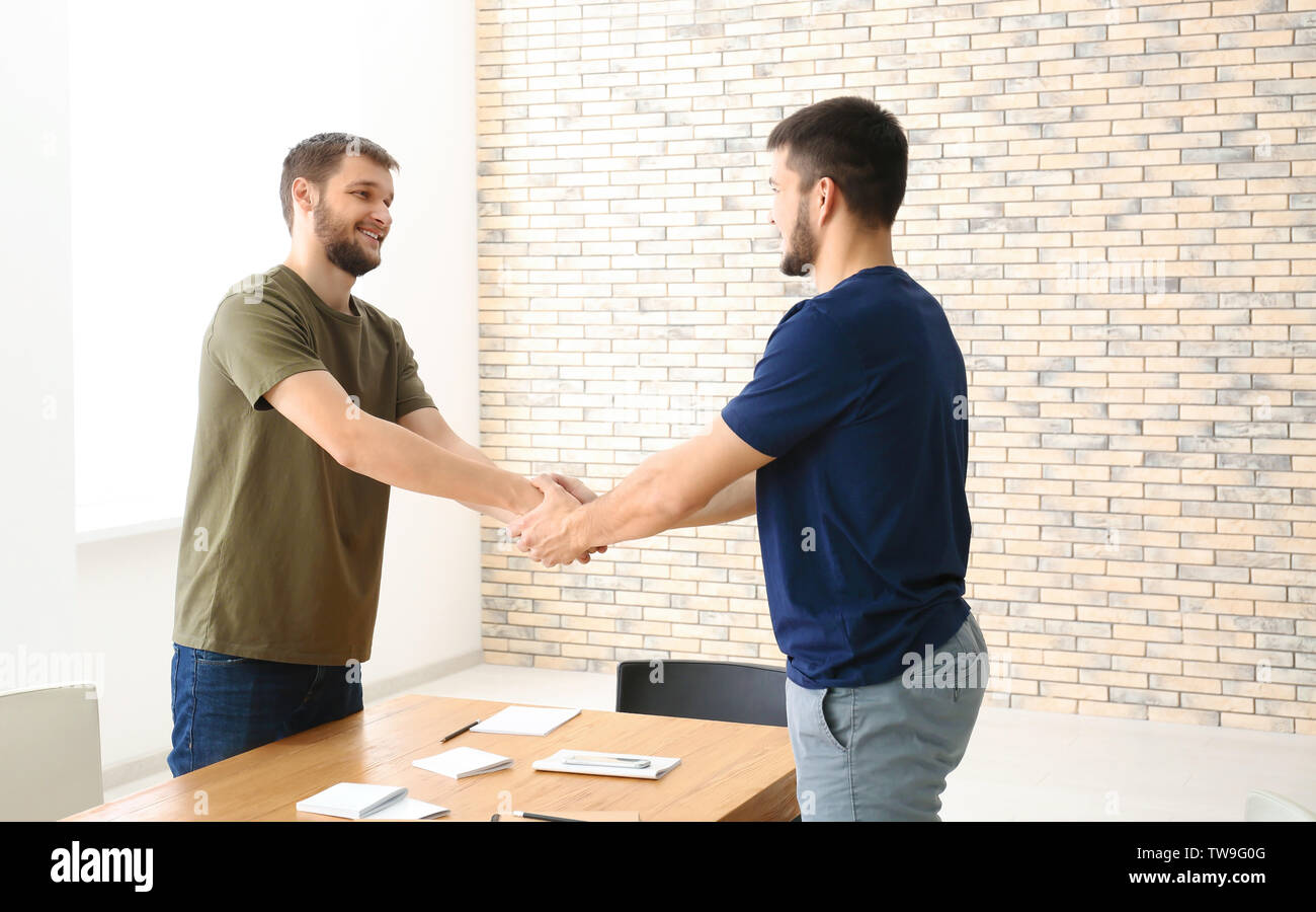 Two young men shaking hands over table. Unity concept Stock Photo - Alamy