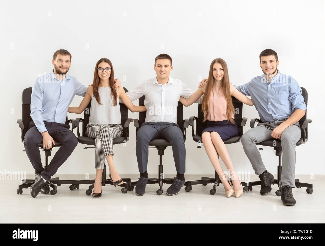 Group of young people sitting together on chairs against white wall ...