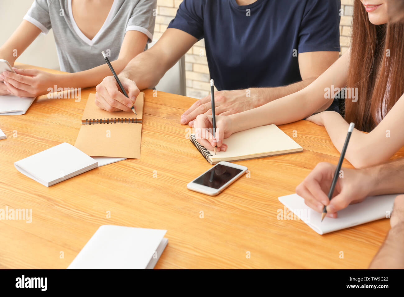 Group of young people writing in notebooks at table, closeup. Unity ...