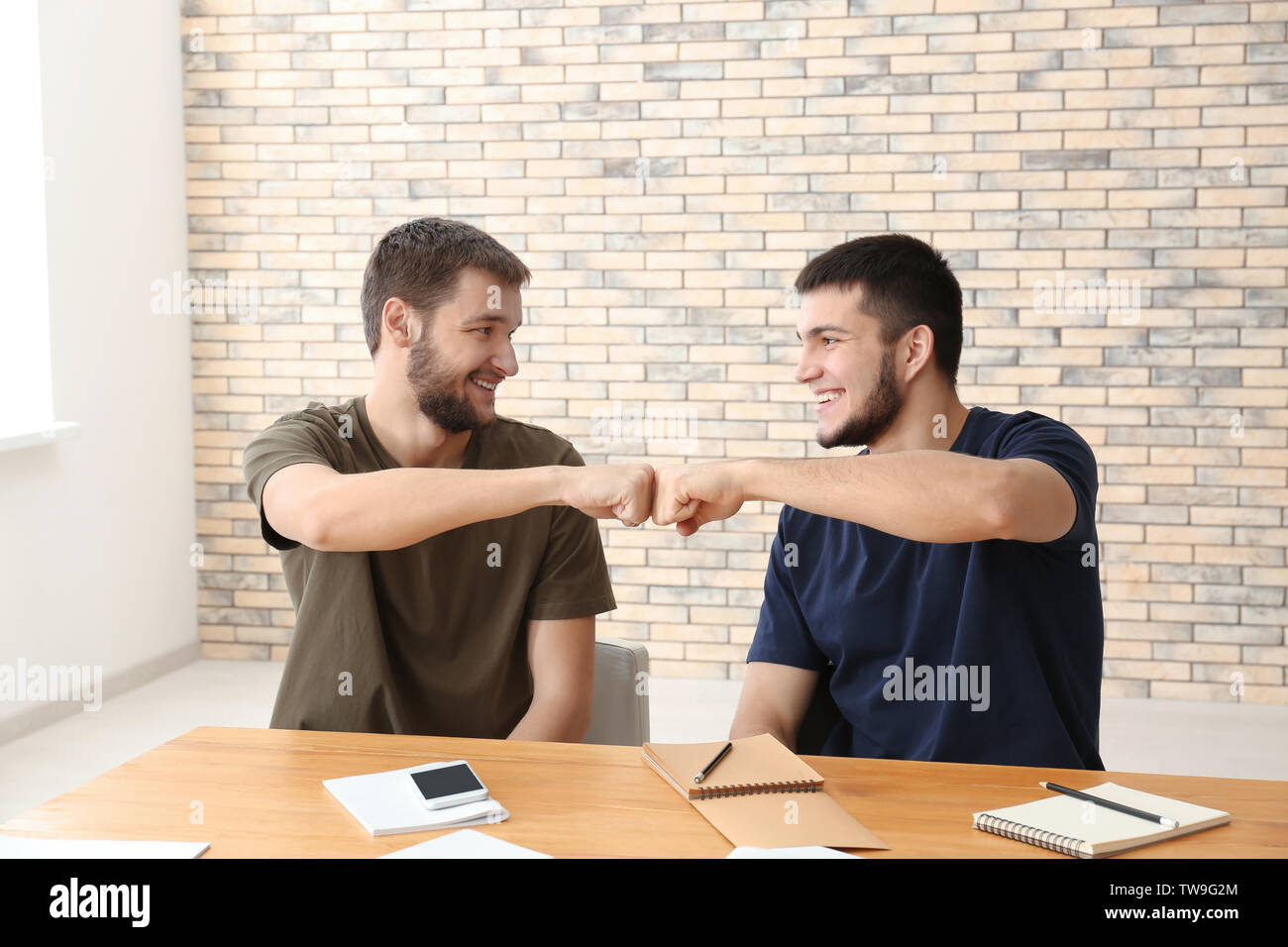 Two young men putting fists together over table. Unity concept Stock ...