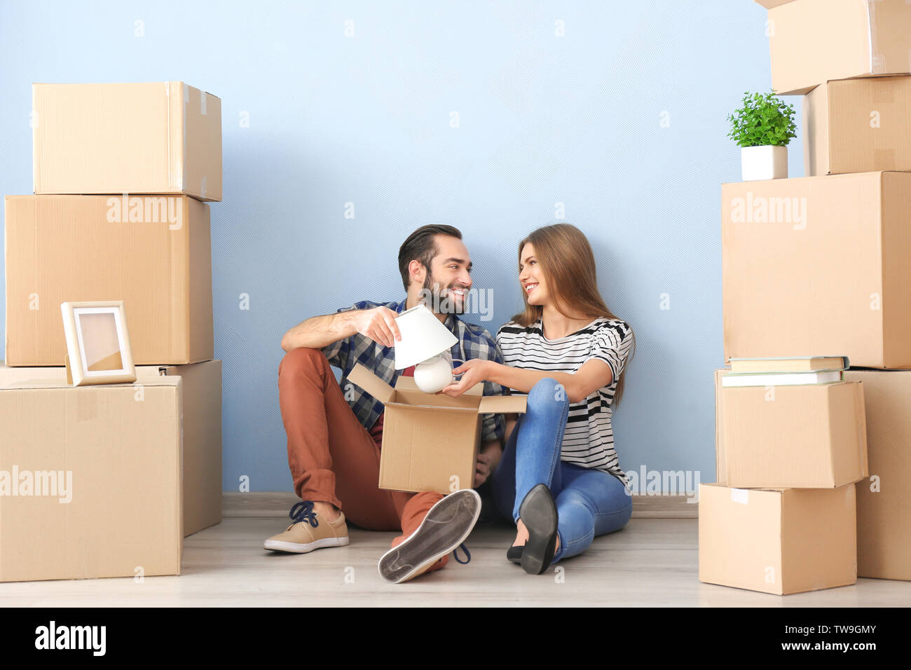 Young couple with moving boxes on floor in room Stock Photo - Alamy