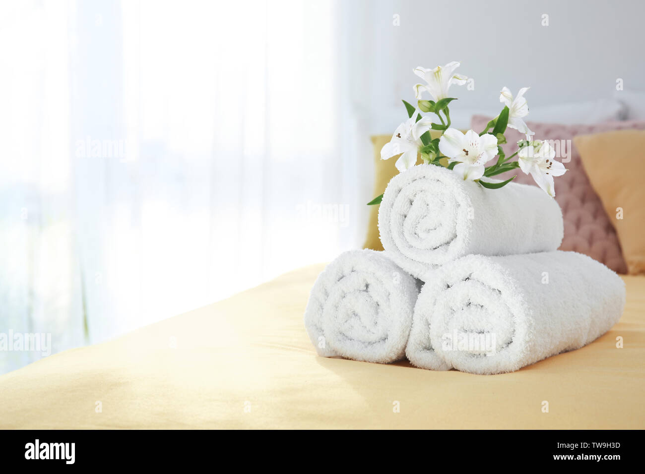Rolled white towels with flowers on bed Stock Photo - Alamy