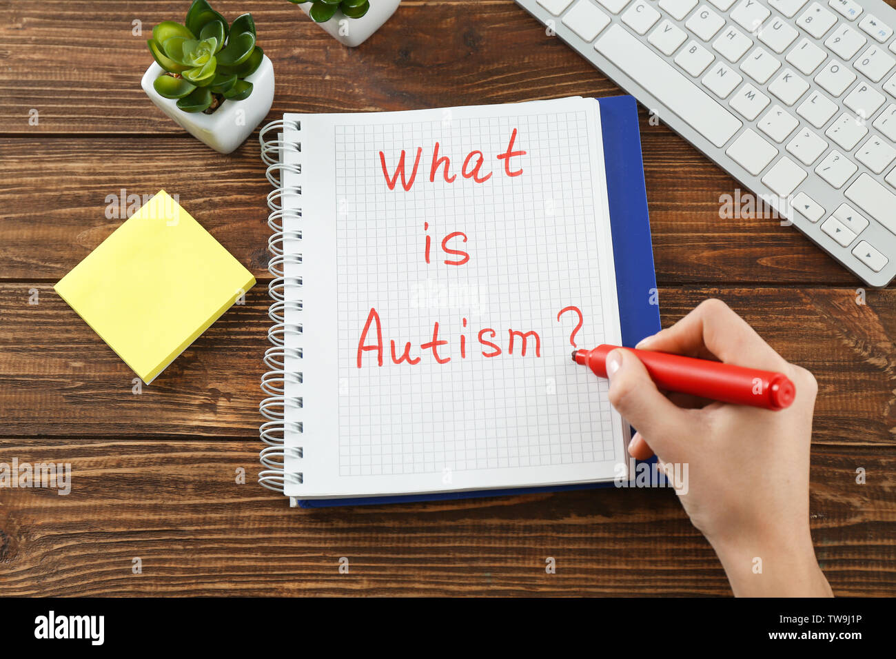 Woman writing text WHAT IS AUTISM? in notepad on wooden background ...