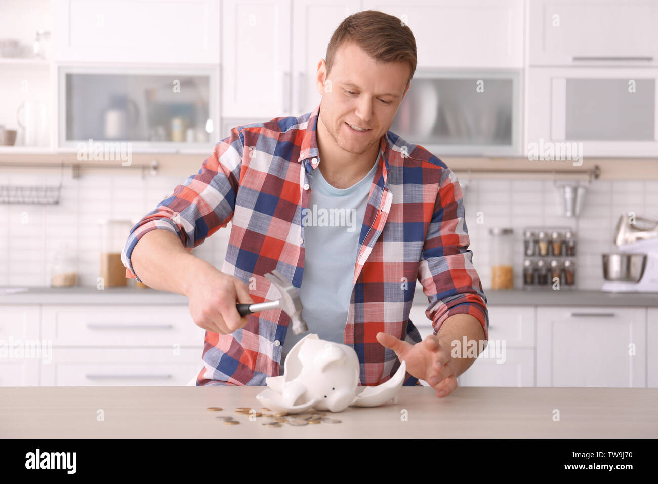 Young man breaking piggy bank with hammer at table indoors Stock Photo ...