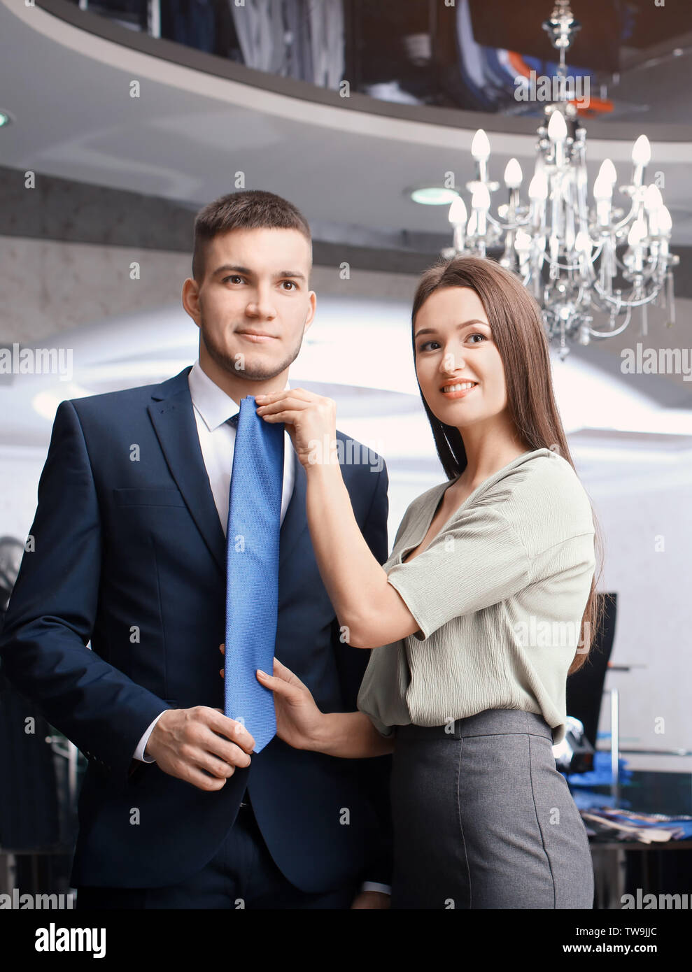 Female shop assistant helping man to choose suit in store Stock Photo ...