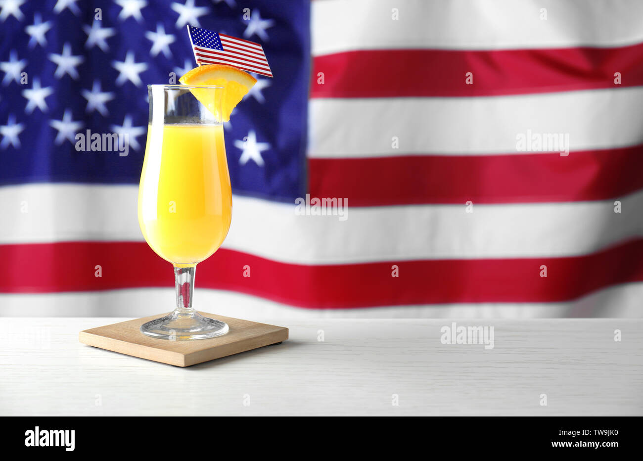 Glass with alcoholic cocktail on table against American flag background ...