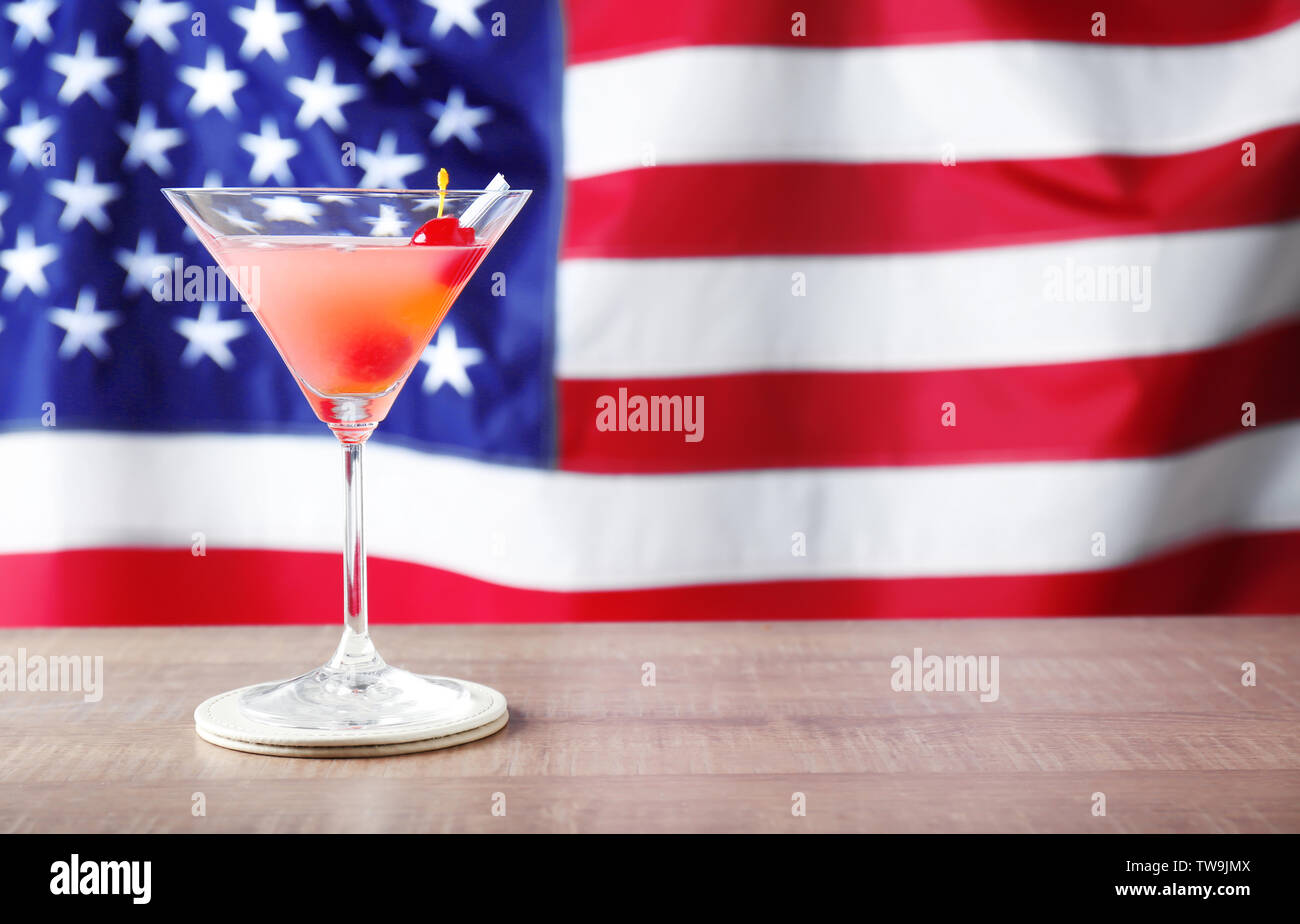 Glass with alcoholic cocktail on table against American flag background ...