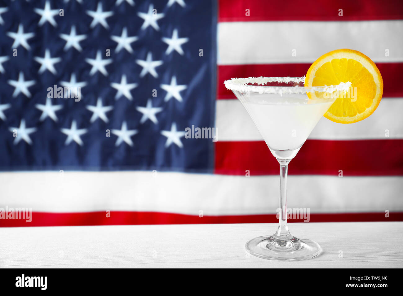 Glass with alcoholic cocktail on table against American flag background ...
