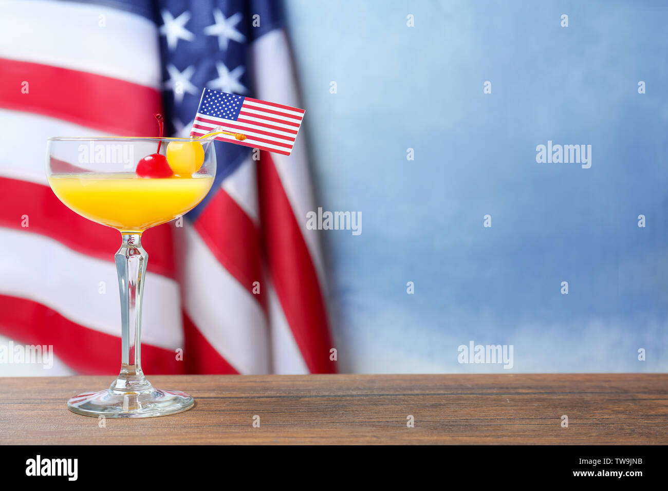 Glass with alcoholic cocktail on table against American flag background ...