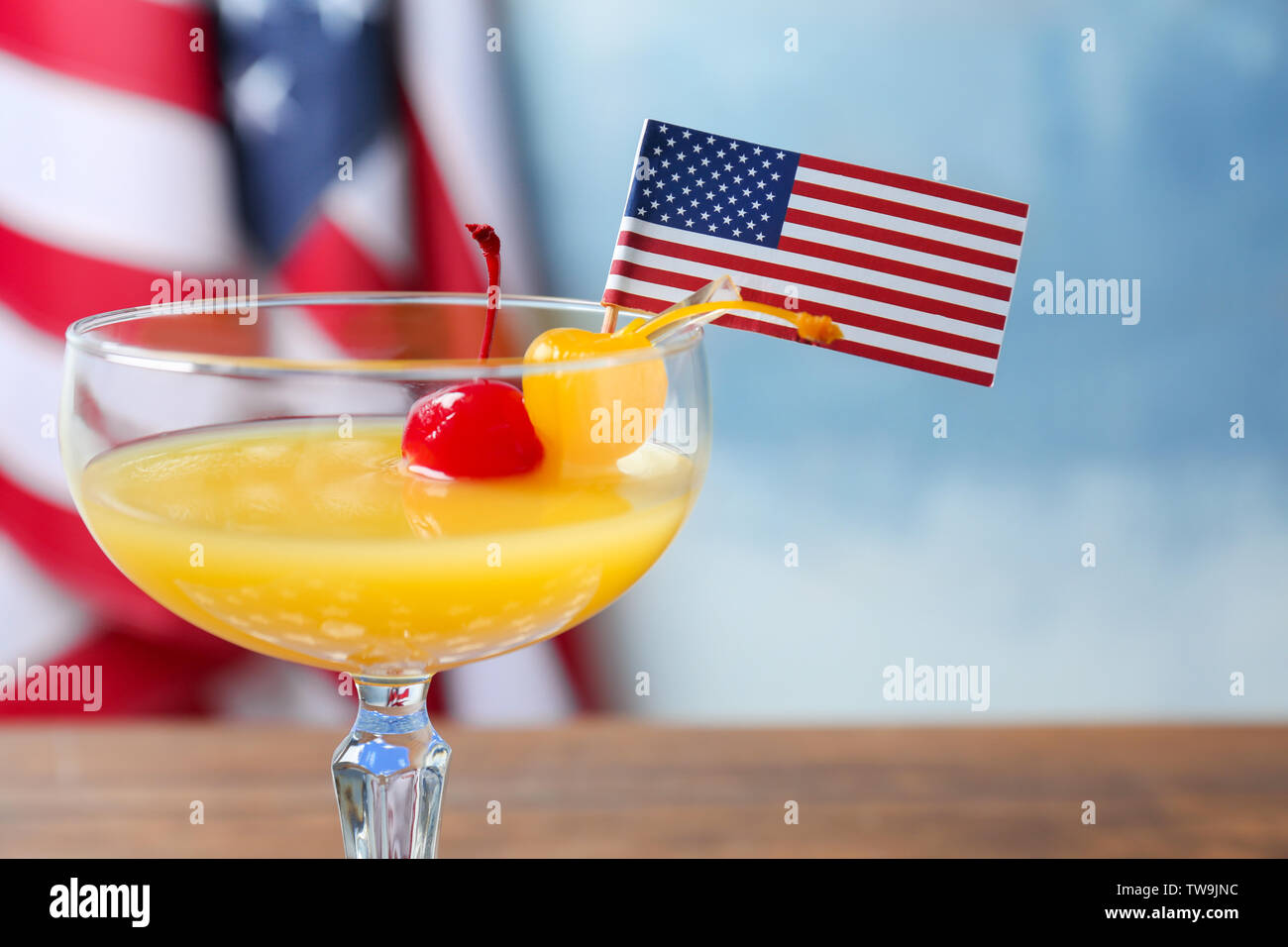 Glass with alcoholic cocktail on table against American flag background ...