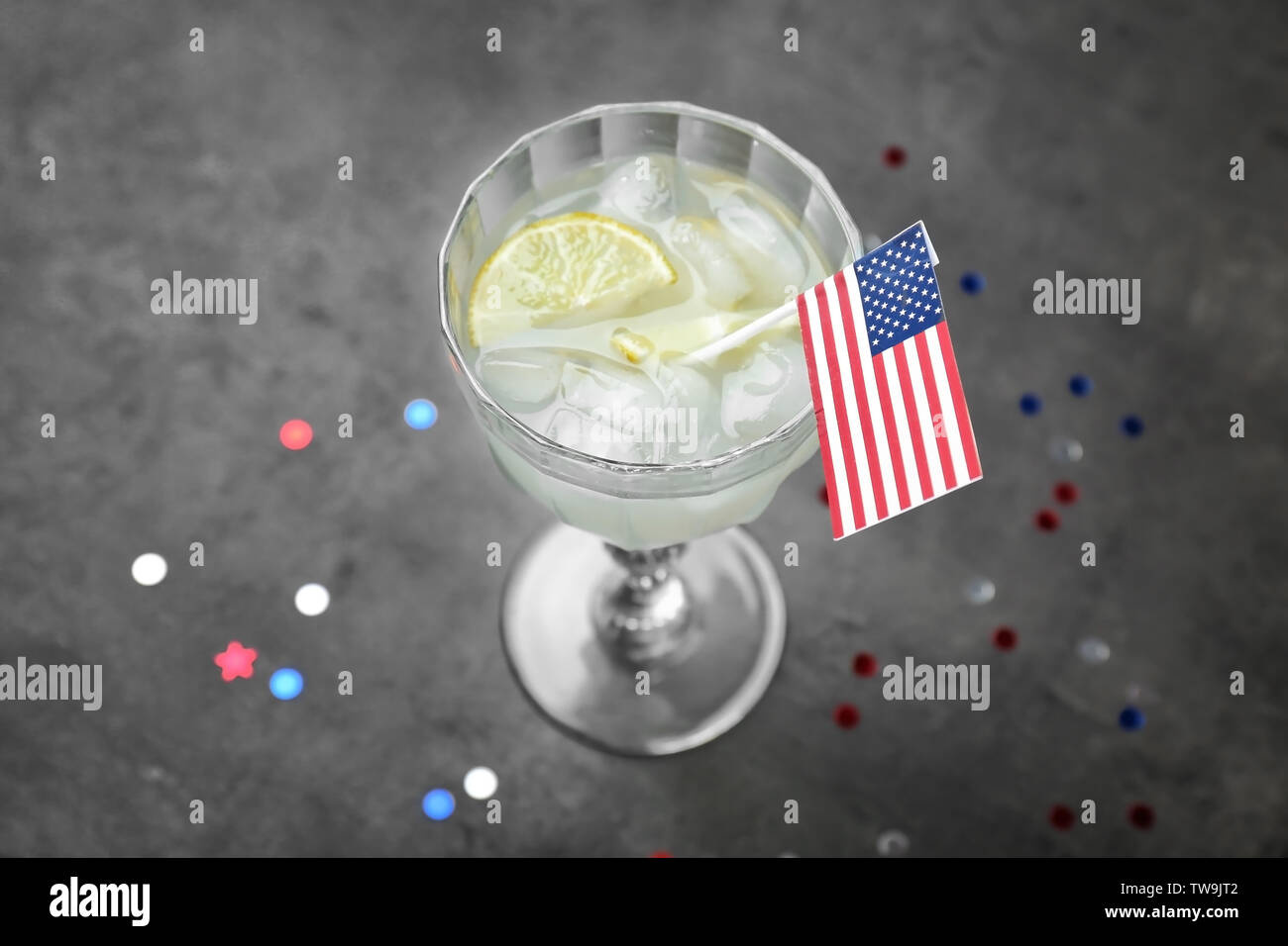 Glass with alcoholic cocktail and small American flag on grey ...