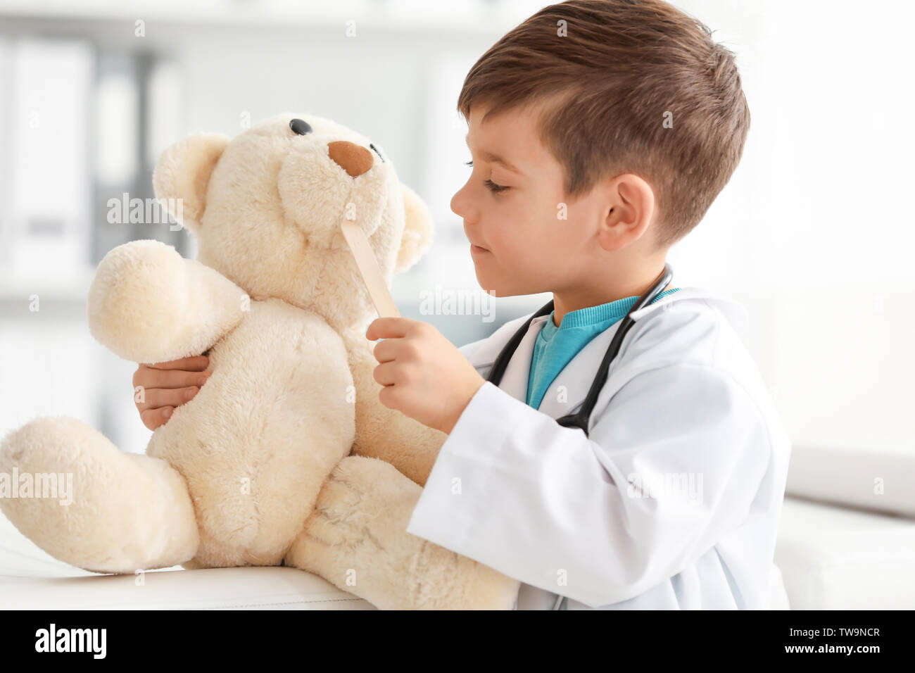Cute little boy dressed as doctor playing with toy bear in hospital ...