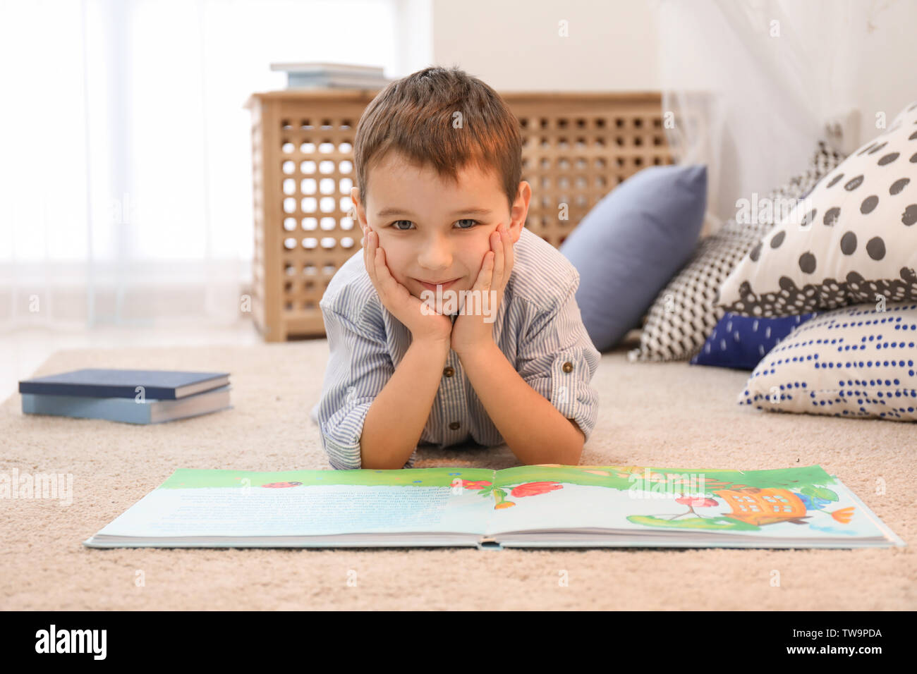 Cute little boy reading book while lying on floor at home Stock Photo ...