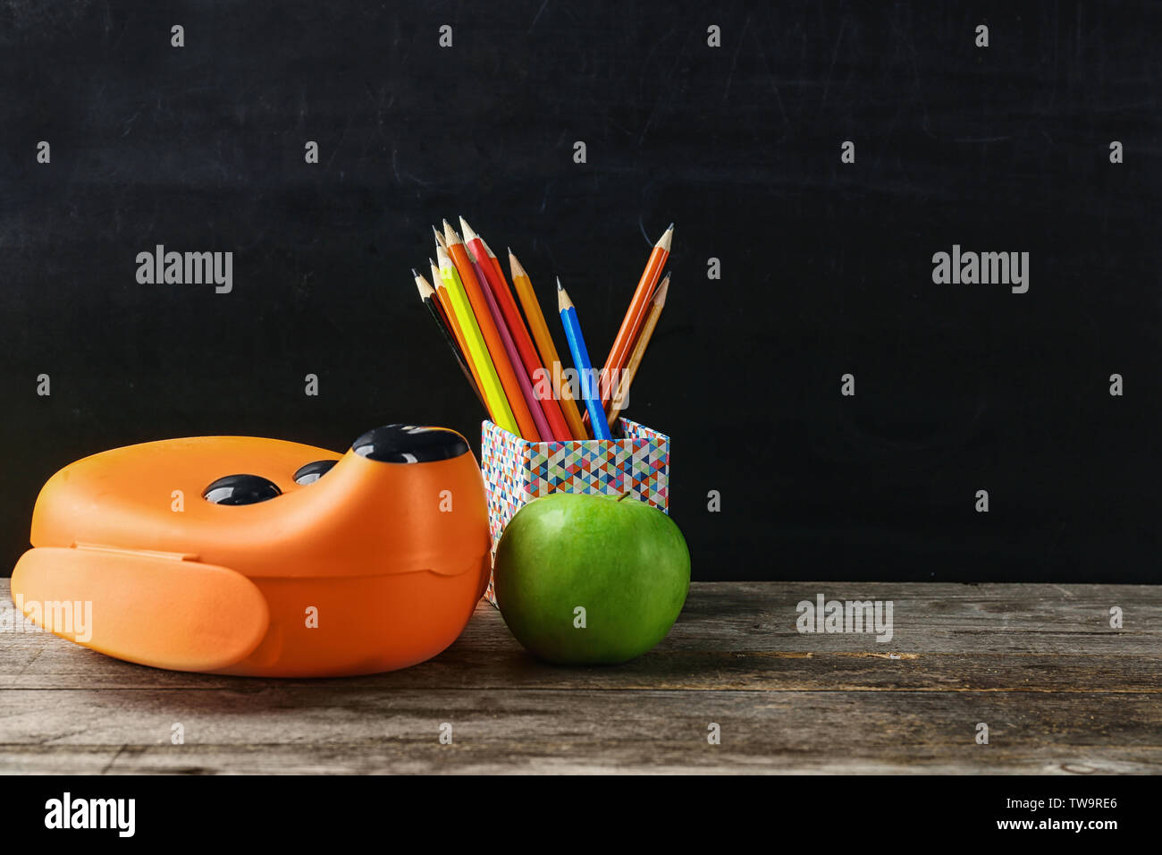Lunch box with food for schoolchild and pencils in holder on dark ...