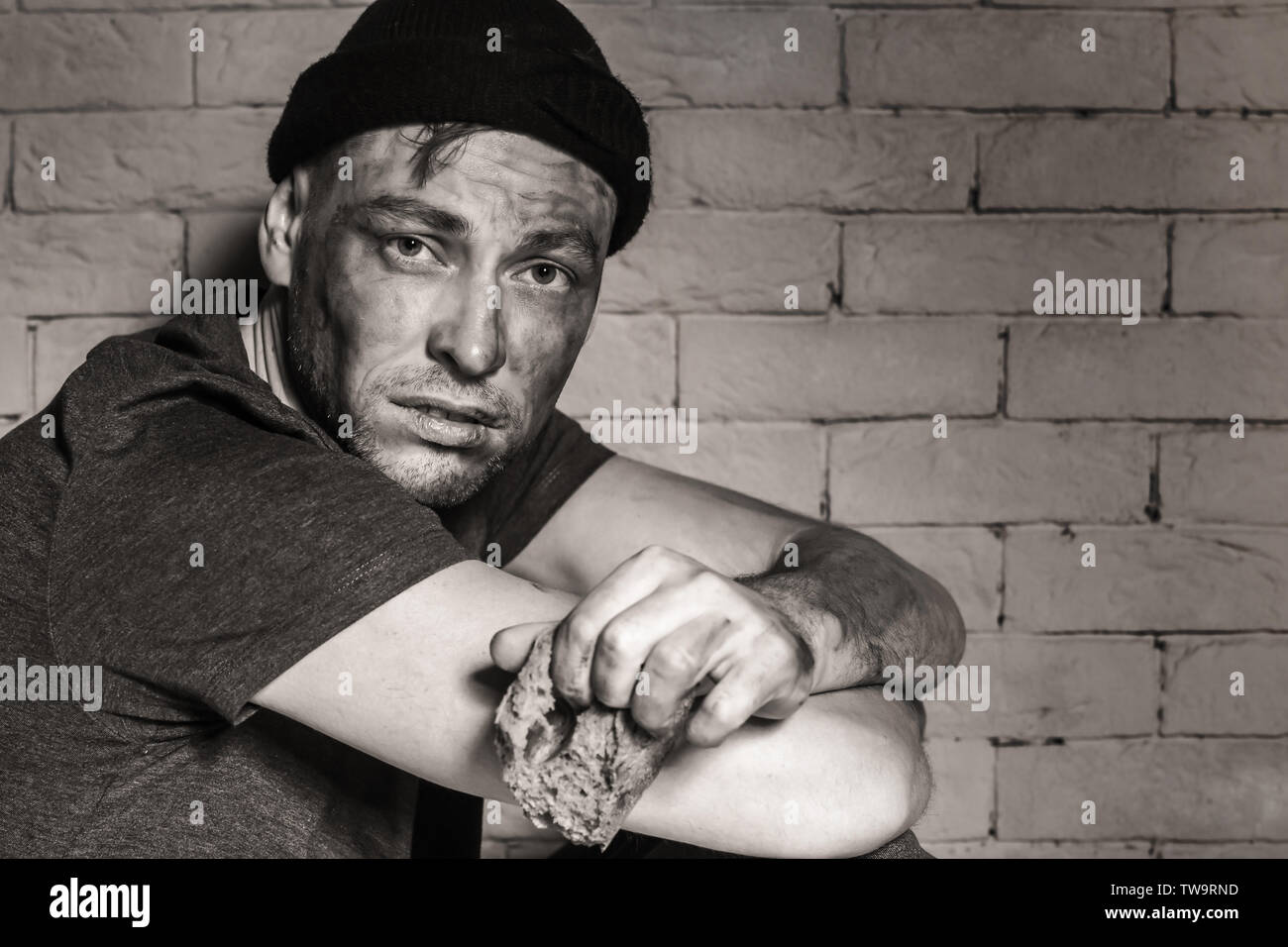 Hungry poor man with piece of bread near brick wall Stock Photo - Alamy