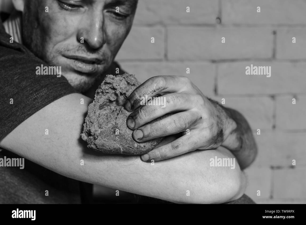 Hungry poor man with piece of bread near brick wall Stock Photo - Alamy