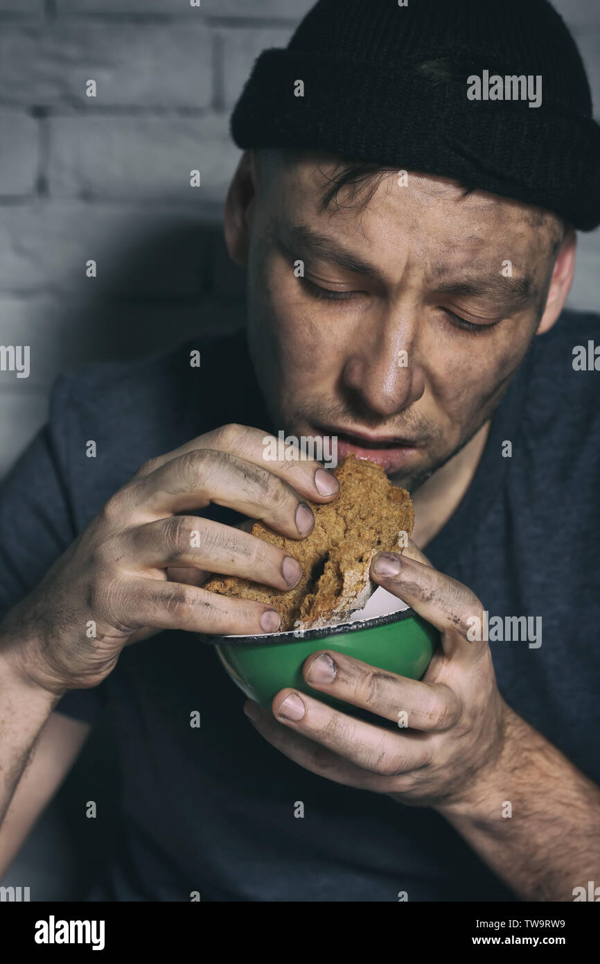 Hungry poor man eating piece of bread against brick wall Stock Photo ...