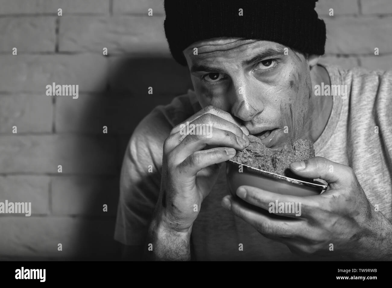 Hungry poor man eating piece of bread near brick wall Stock Photo - Alamy