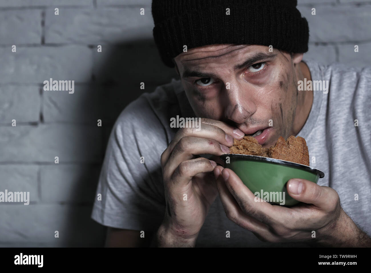 Hungry poor man eating piece of bread near brick wall Stock Photo - Alamy
