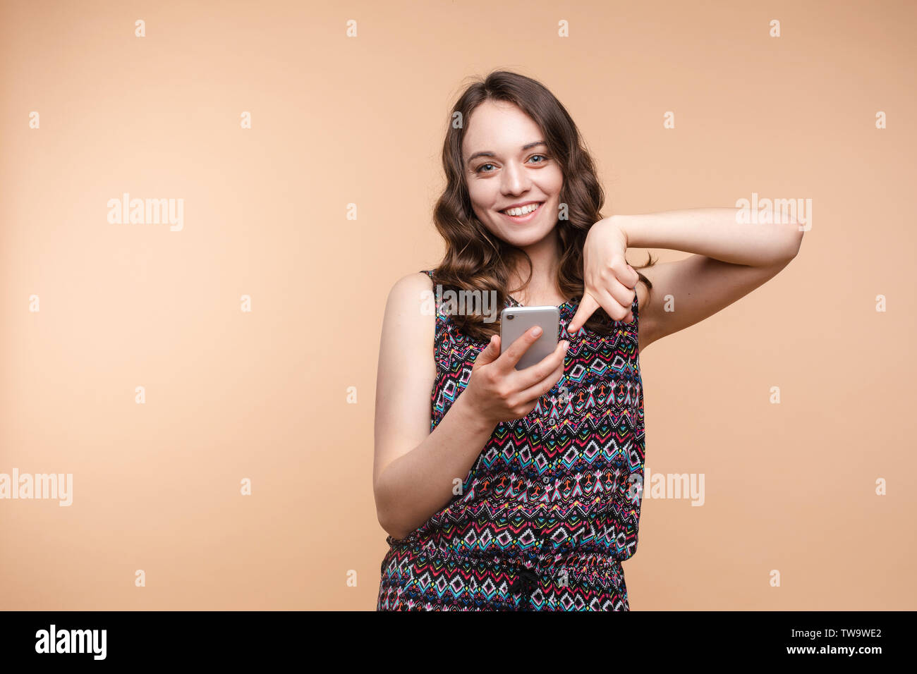 Pretty girl pointing at cell phone.Studio portrait of beautiful ...