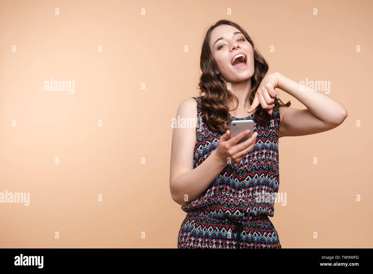 Pretty girl pointing at cell phone.Studio portrait of beautiful ...