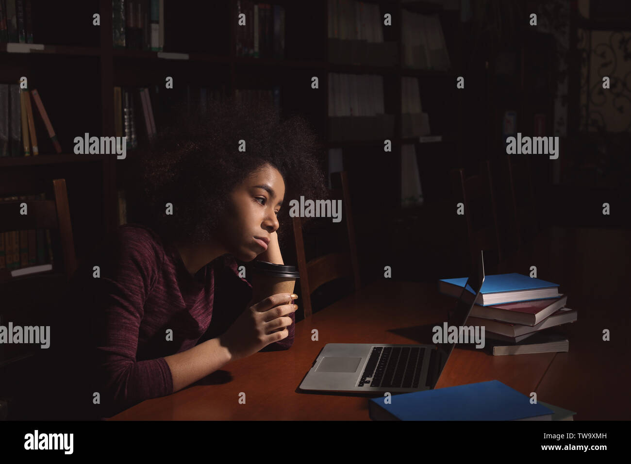 African American student with laptop studying in library late at night ...